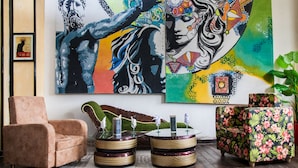 Uma sala de estar moderna com uma poltrona rosa, duas mesas redondas com bases decorativas e um sofá estampado com motivos florais.