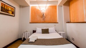 Quarto de hotel com cama, duas mesas de cabeceira, um quadro na parede e uma luminária de teto singular.
