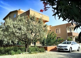 Um edifício de vários andares com uma bandeira, rodeado por árvores e um carro estacionado.
