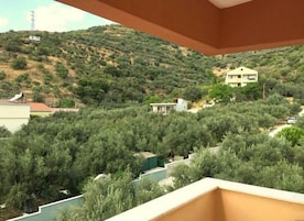 Varanda com vista para uma encosta com vegetação escassa e alguns edifícios.