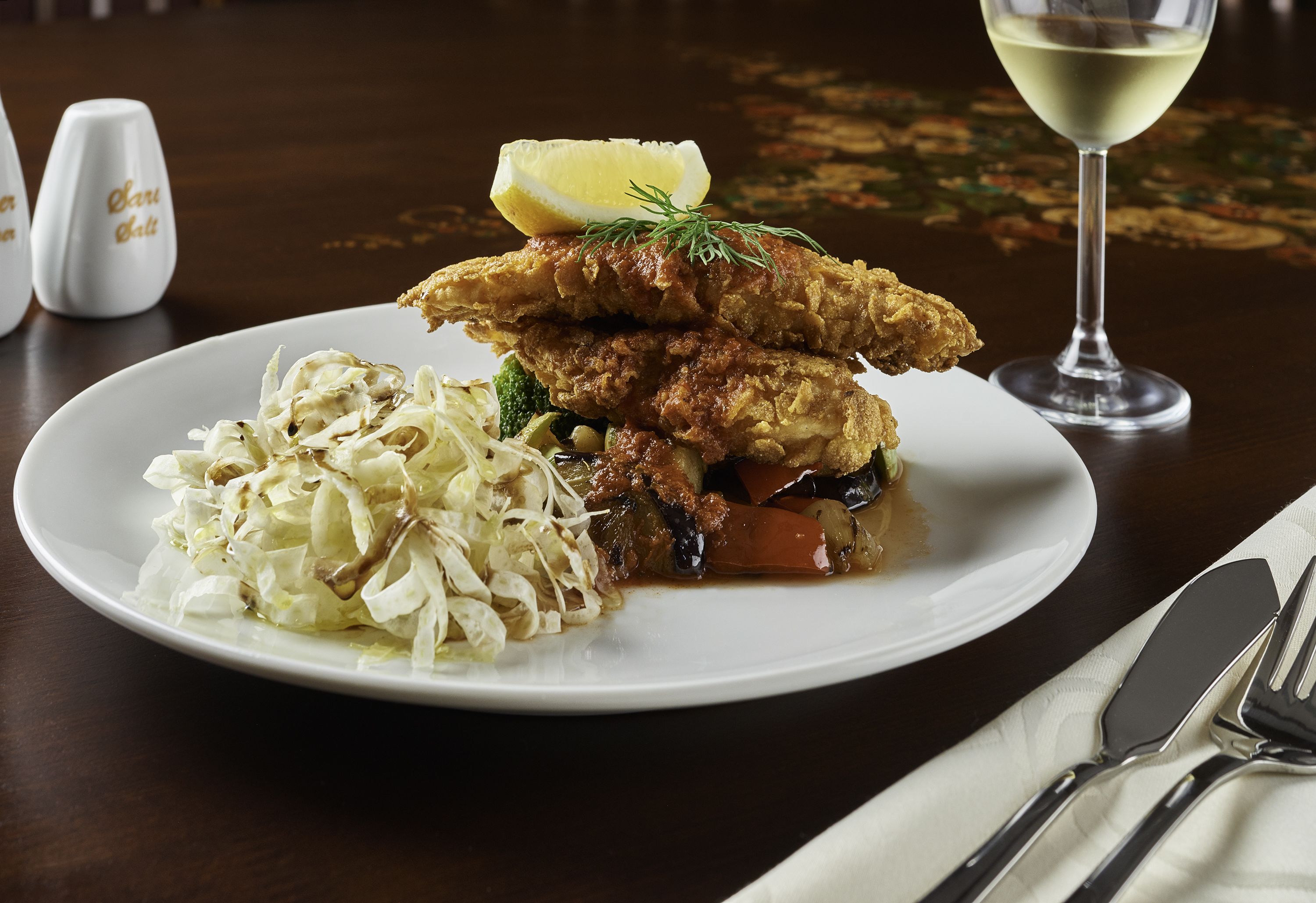 Prato de peixe frito com limão e endro, acompanhado de salada de repolho e legumes.