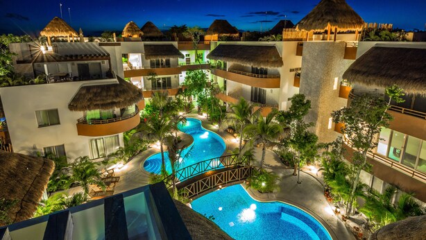 Um resort com vários edifícios, uma piscina central e estruturas com telhados de palha.