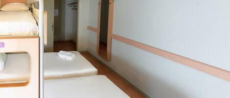 Quarto de hotel compacto com beliches, banheiro pequeno e um espelho.