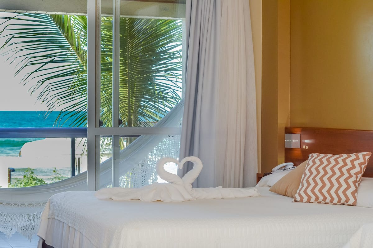 Quarto de hotel com cama, toalha em formato de coração, telefone e vista para o oceano.