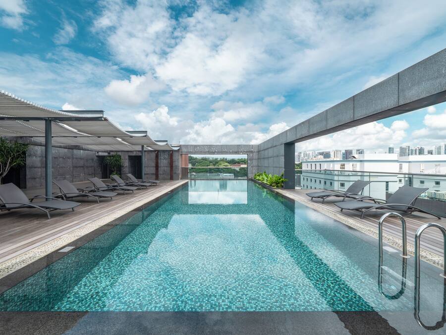 Piscina infinita no terraço com espreguiçadeiras, céu claro e vista para a cidade.