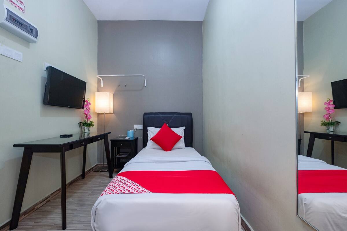 Quarto de hotel com cama, escrivaninha, cadeira, televisão e espelho.