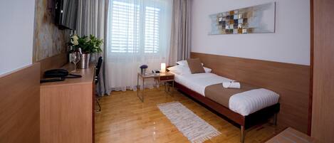 Quarto de hotel com cama, escrivaninha, televisão, janela com cortinas e um quadro na parede.