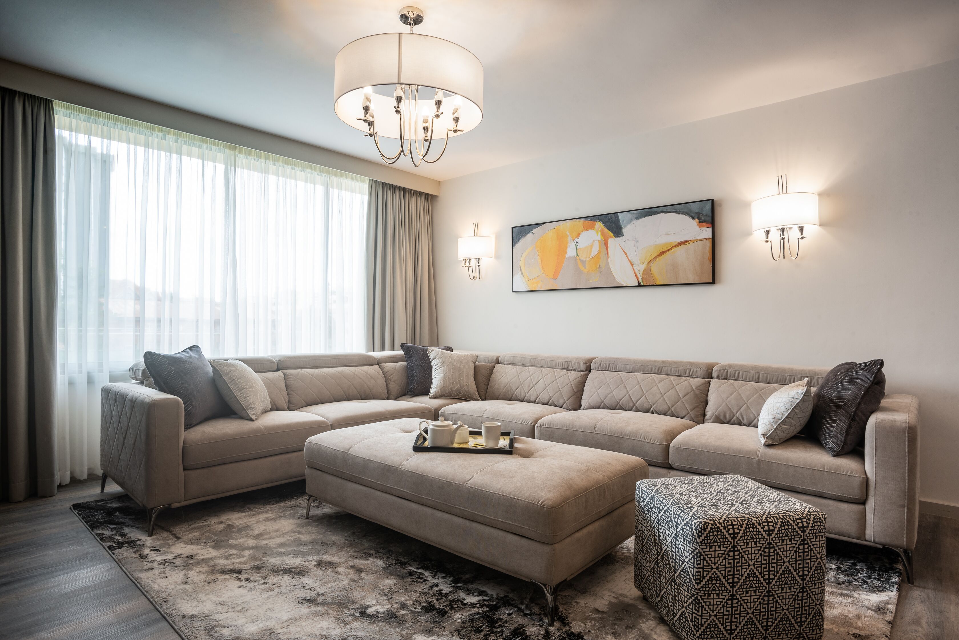 Uma sala de estar moderna com sofá seccional, um banquinho combinando e um candelabro.