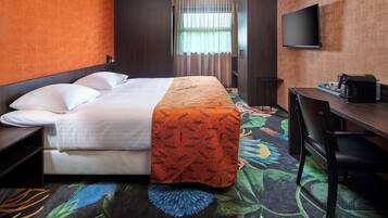 Quarto de hotel com cama, escrivaninha, cadeira, televisão e janela com cortinas.