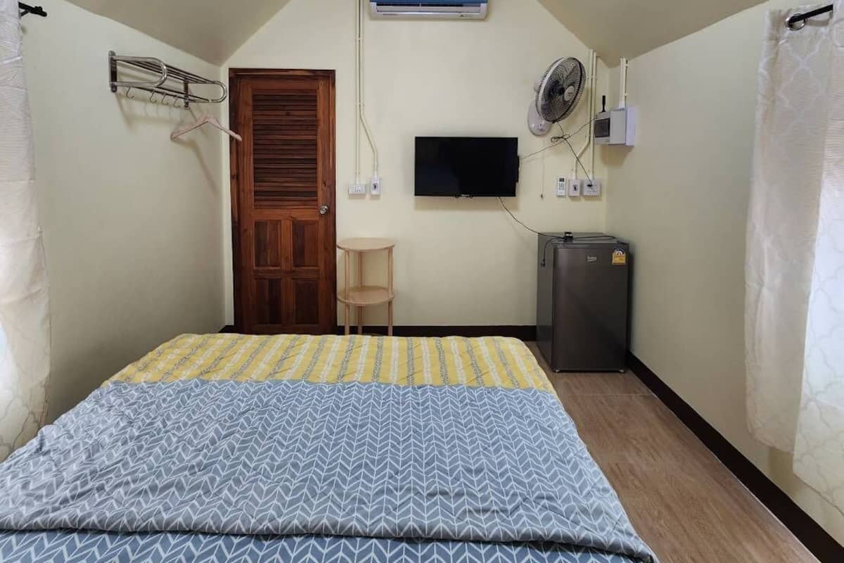 Um quarto pequeno e bem iluminado, com uma cama, uma televisão, ar condicionado e ventilador.