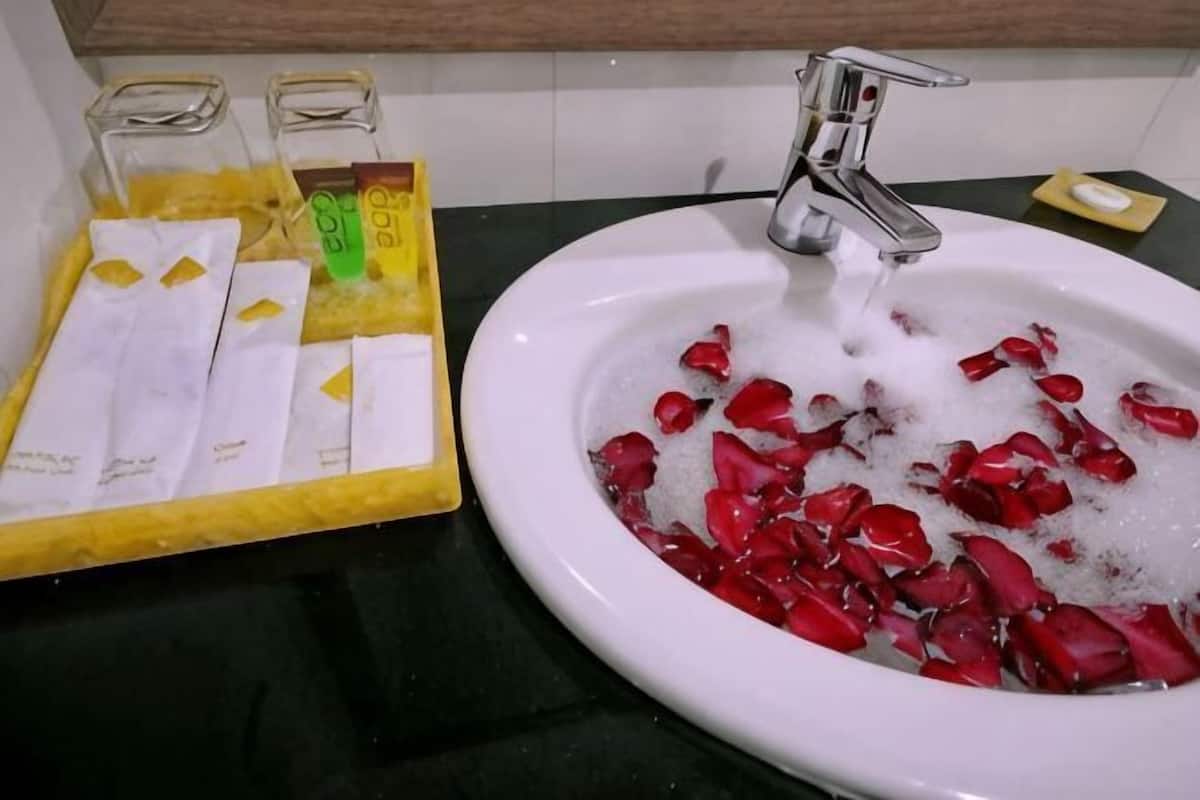 Uma pia com pétalas de rosa, um descanso com artigos de higiene e um saboneteira.