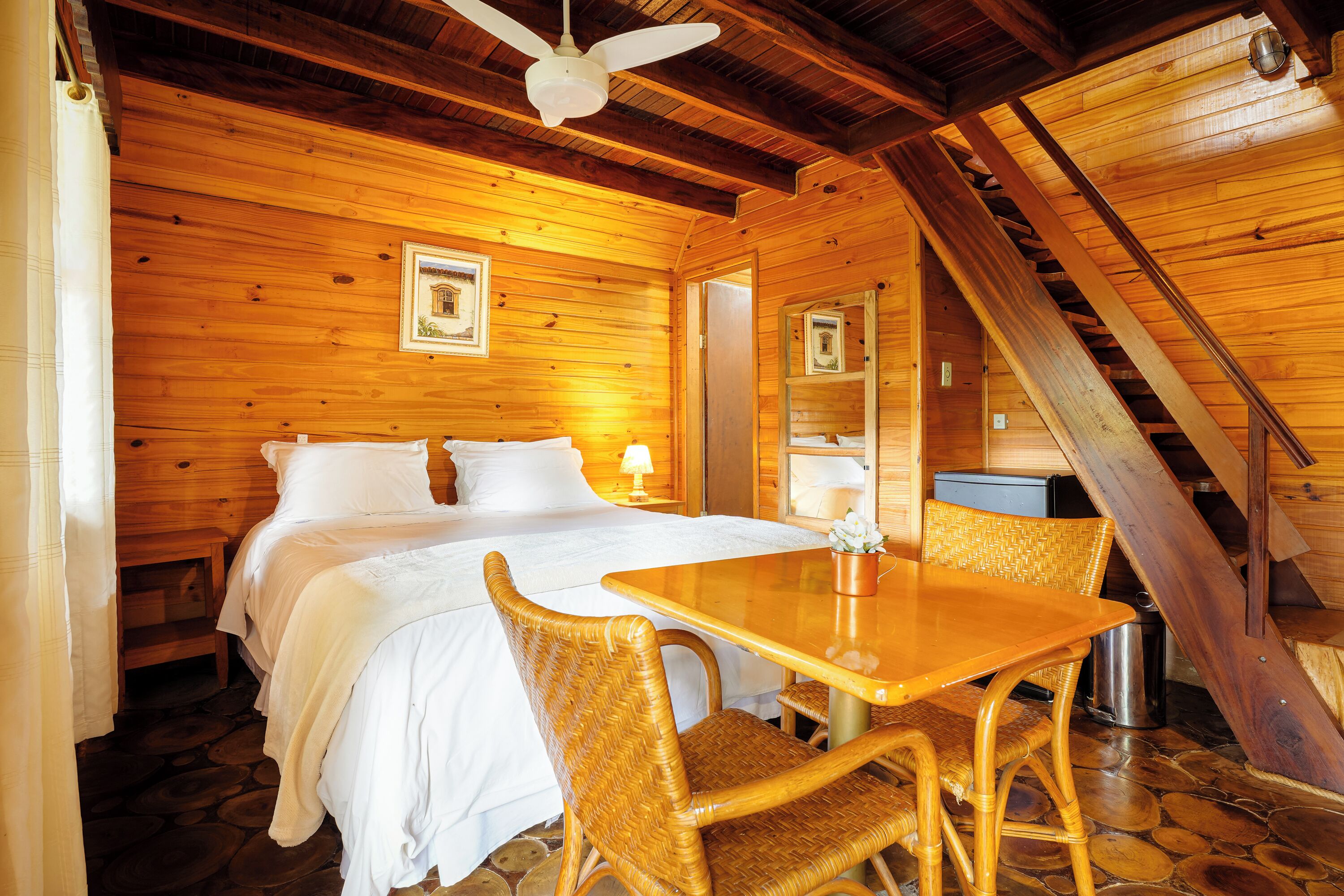 Quarto de cabana de madeira com cama, mesa e cadeiras de vime.