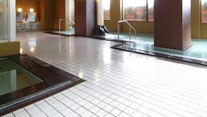 Uma piscina interior ampla com paredes de vidro transparente, chão de azulejos e vista para o exterior.
