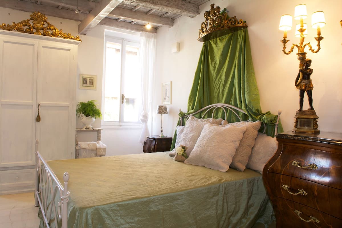 Quarto com cama, penteadeira, dossel verde e candelabro.