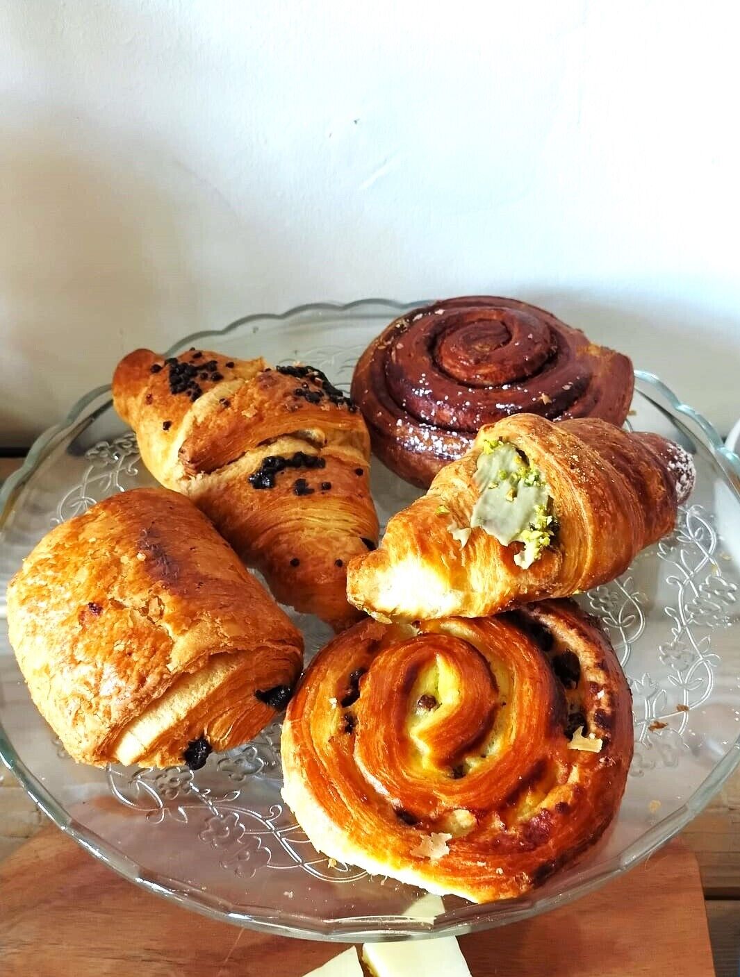 Uma travessa de vidro com diversos doces, incluindo um croissant e um cinnamon roll.