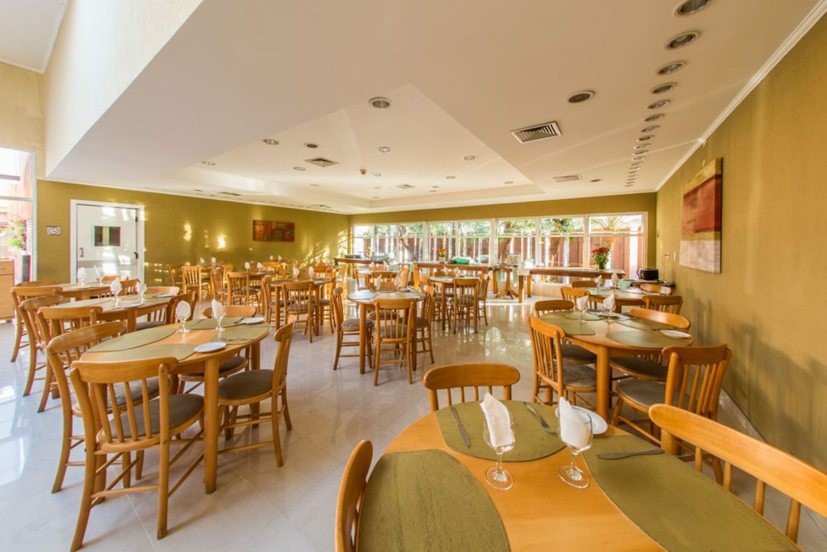 Uma ampla sala de jantar com várias mesas e cadeiras, dispostas em um ambiente informal.