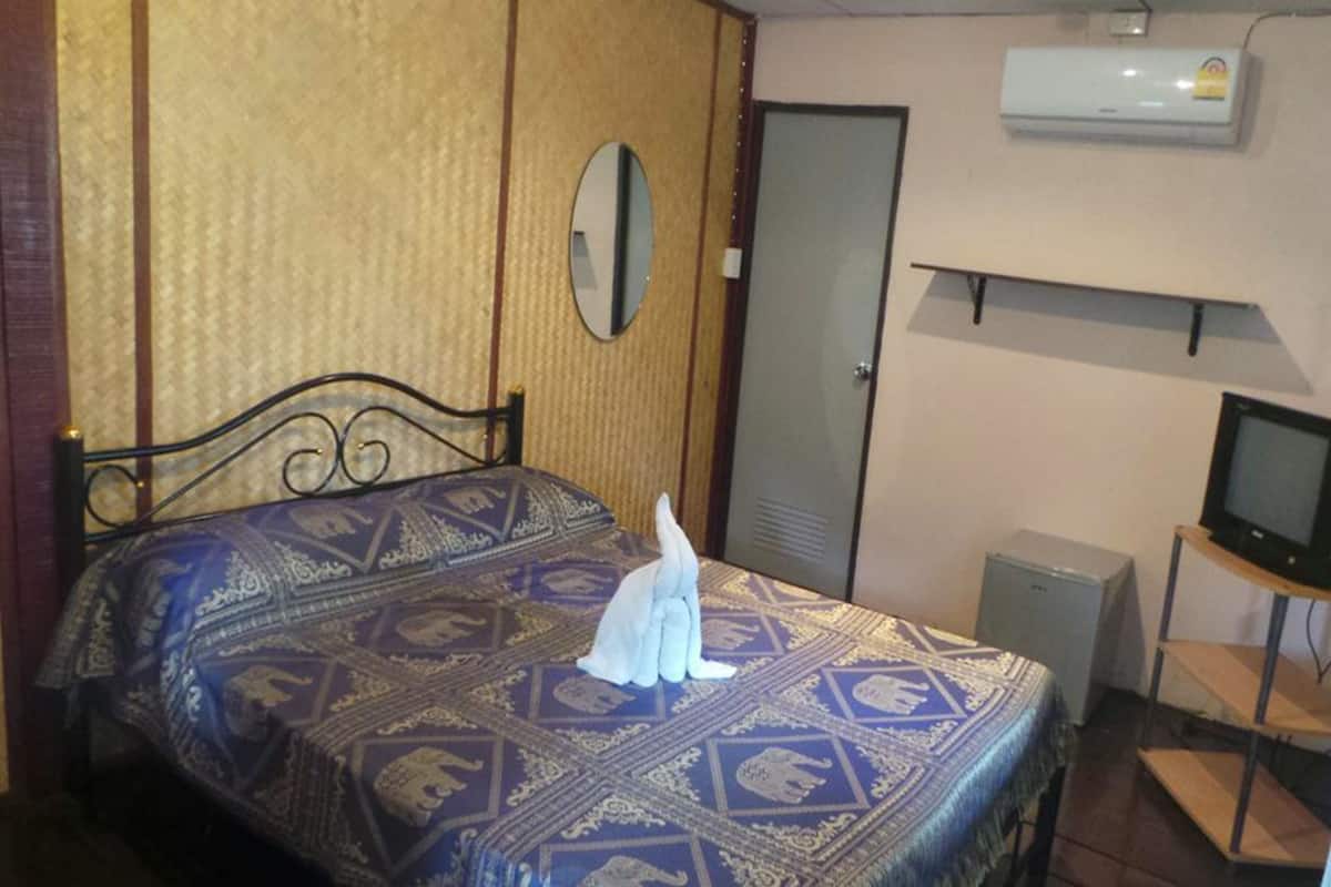 Quarto de hotel com colcha estampada, espelho na parede, aparelho de ar condicionado, televisão em um suporte e um pequeno armário.