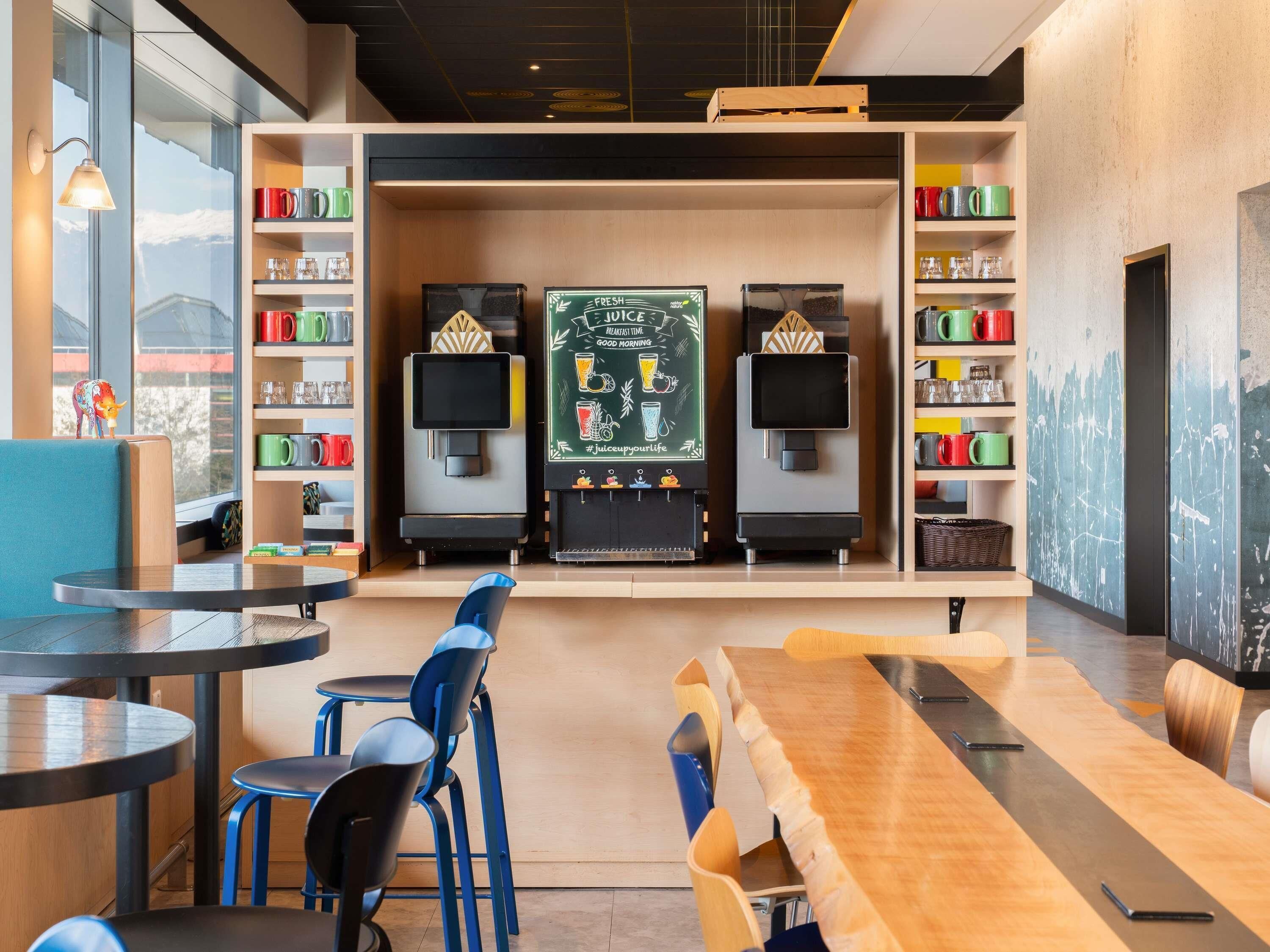 Um café moderno com duas máquinas de expresso, áreas de estar e estantes com canecas.