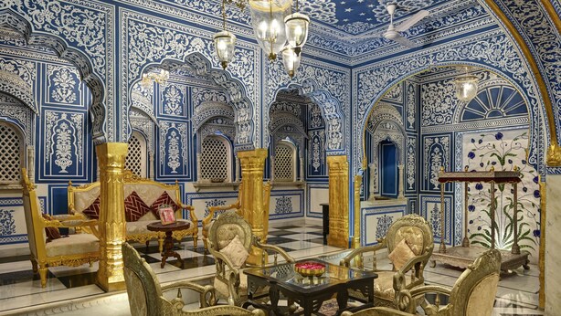 Um quarto luxuoso com decoração azul e dourada detalhada, um candelabro e piso xadrez.