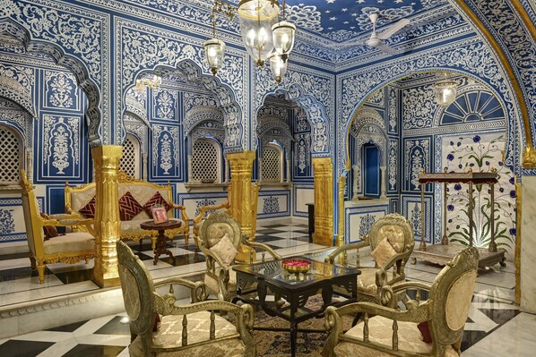 Um quarto luxuoso com decoração azul e dourada detalhada, um candelabro e piso xadrez.