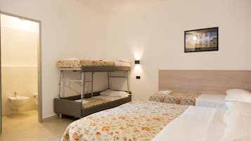 Quarto de hotel com duas camas, uma beliche e outra com duas camas de solteiro. Banheiro com pia e vaso sanitário visíveis.