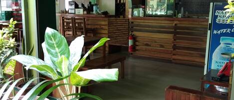 Restaurante com interior em madeira, balcão com menu e plantas em vasos.