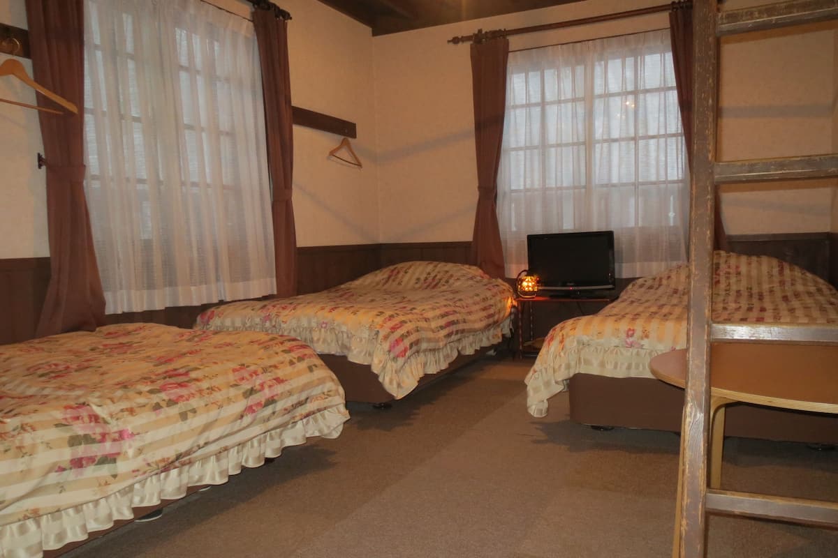 Quarto com duas camas de solteiro, televisão sobre uma mesinha e uma cadeira de madeira.