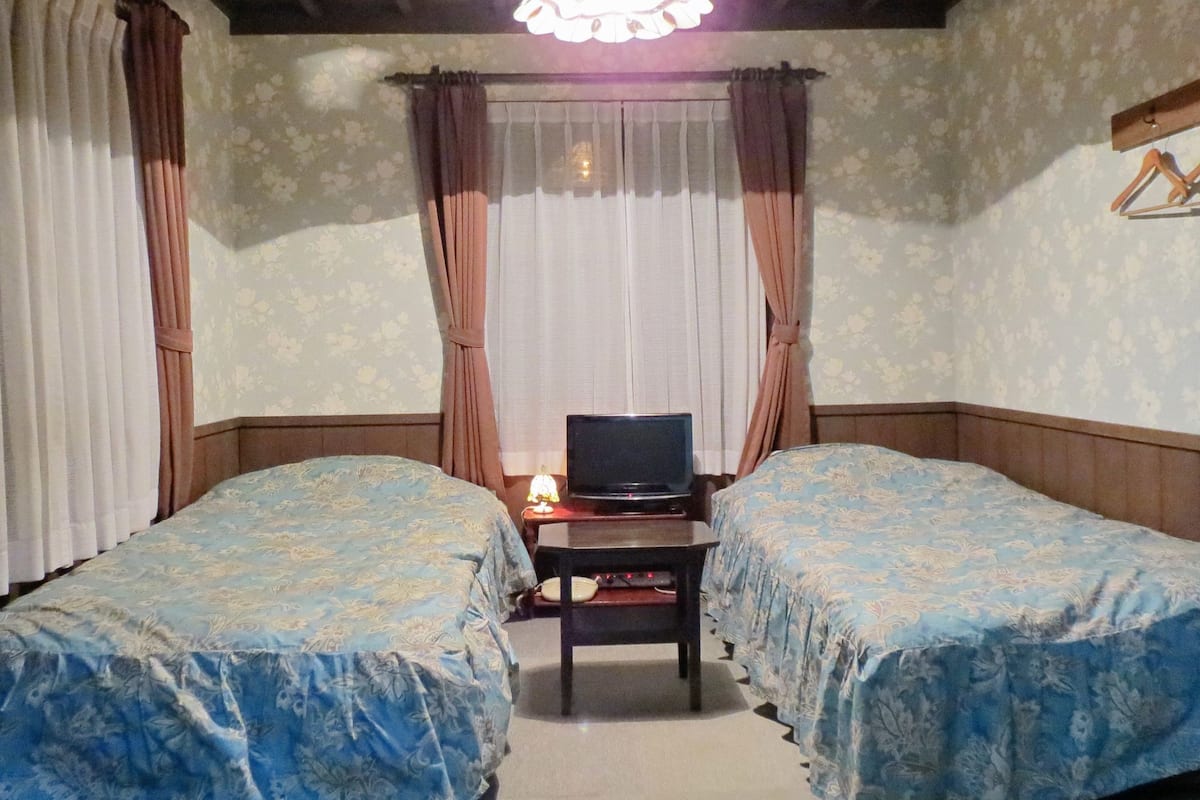 Quarto com duas camas, uma escrivaninha com um laptop e um candelabro.