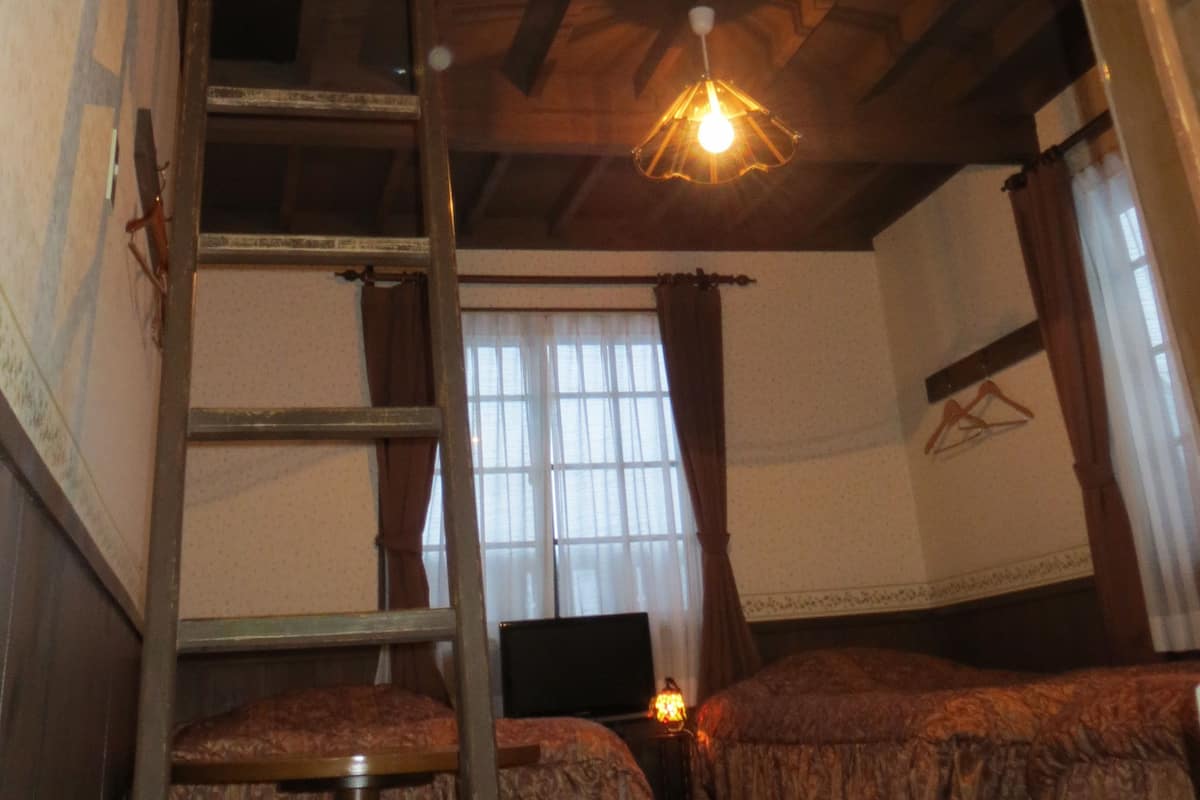 Um quarto com escada de madeira, duas camas com roupa de cama estampada, uma televisão e um ventilador de teto.