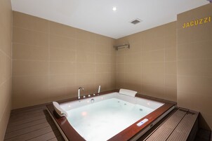 Um banheiro moderno com uma banheira grande, piso de madeira e azulejos bege.