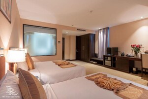 Quarto de hotel com duas camas, uma escrivaninha, televisão e uma janela grande.
