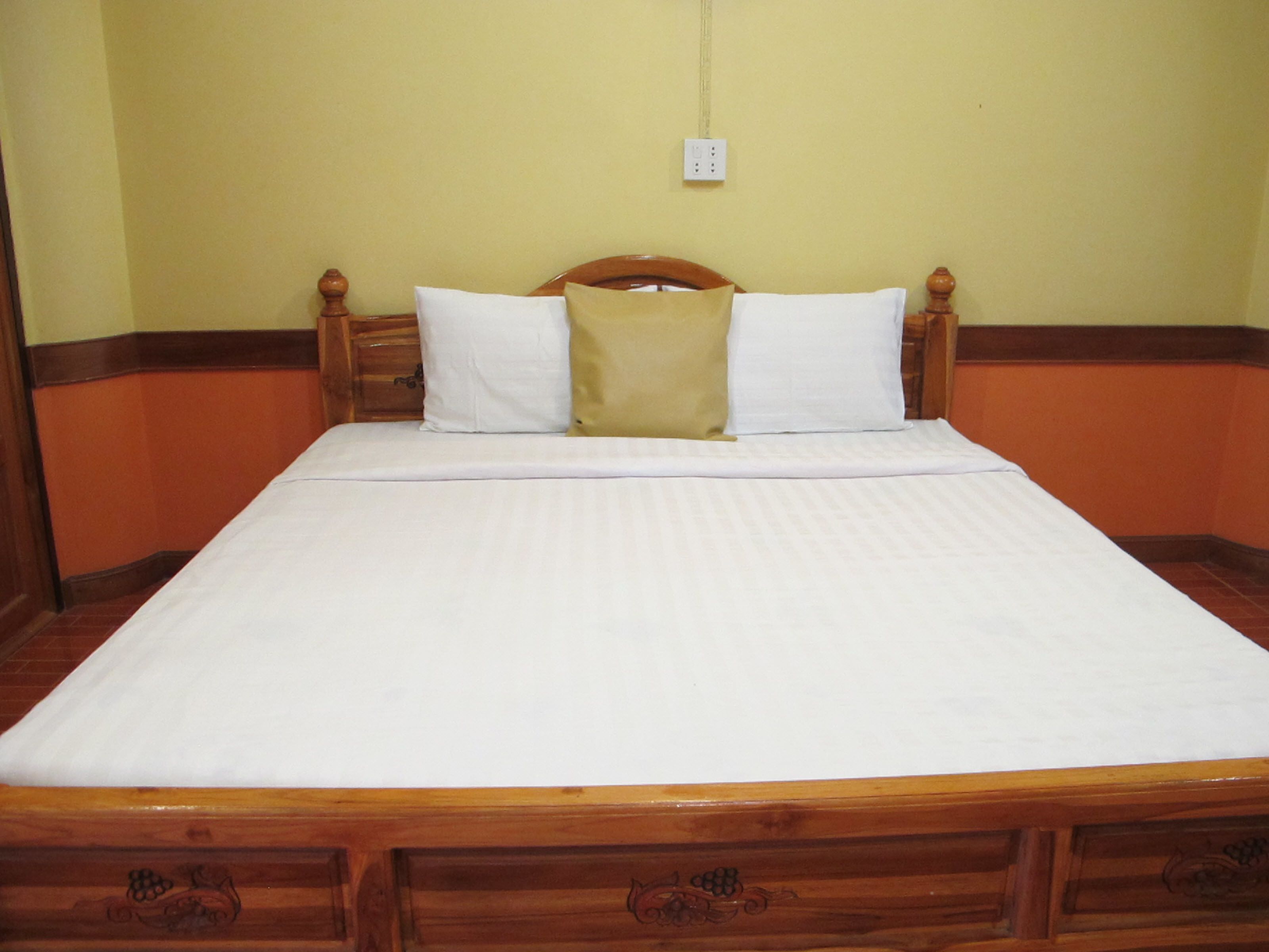 Uma cama de solteiro com estrutura e cabeceira de madeira, roupa de cama branca e travesseiro bege.