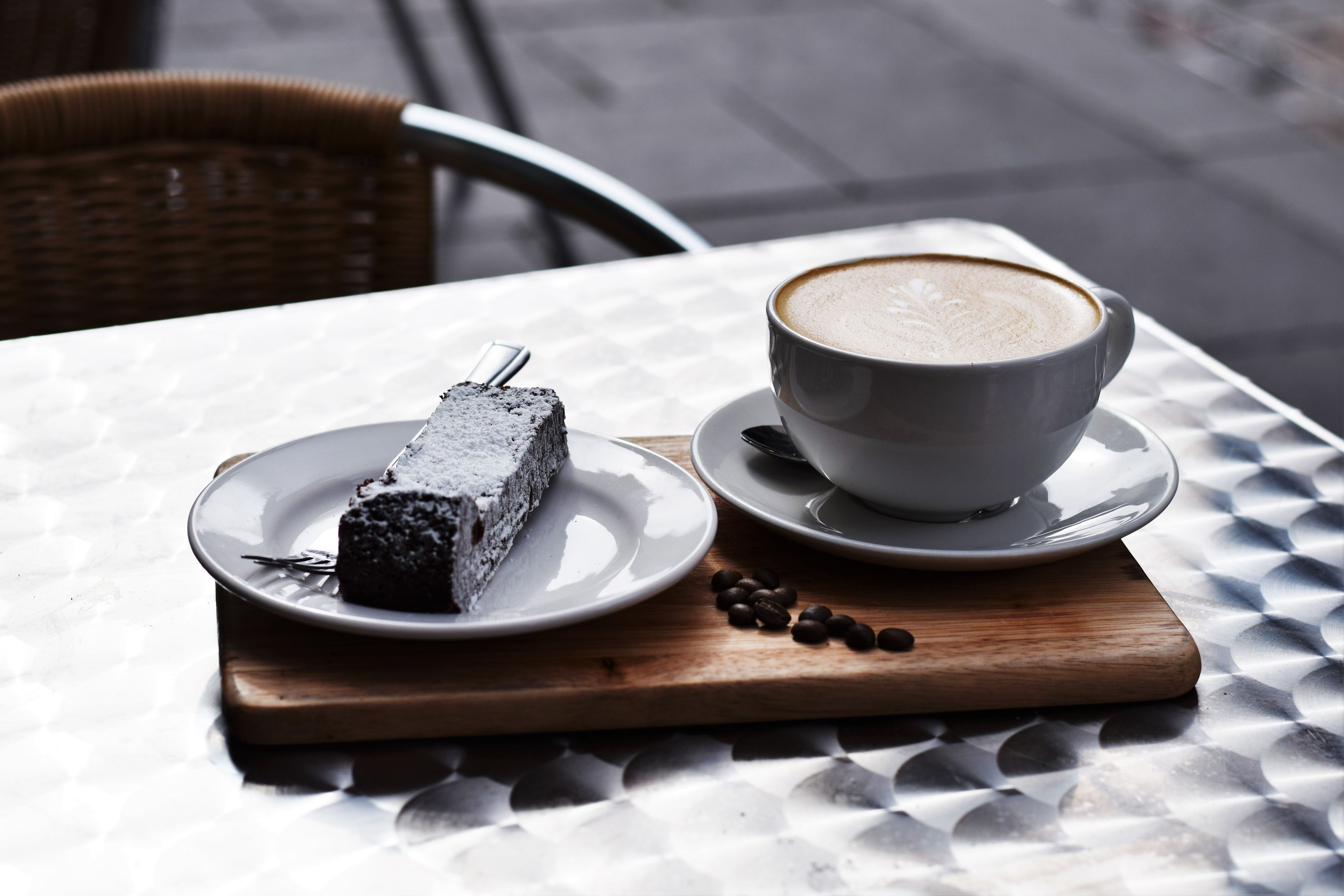 Uma mesa com um prato branco que exibe uma fatia de bolo e uma xícara de café sobre uma toalha de mesa estampada.