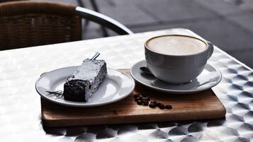 Uma mesa com um prato branco que exibe uma fatia de bolo e uma xícara de café sobre uma toalha de mesa estampada.