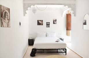 Quarto minimalista com cama, mesa de cabeceira, mala e obras de arte na parede.