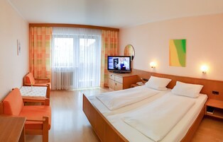 Quarto de hotel com duas camas, uma escrivaninha, uma cadeira, uma televisão e uma janela com cortinas.
