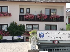 Fachada de hotel com varandas decoradas com flores cor-de-rosa, uma placa com a inscrição