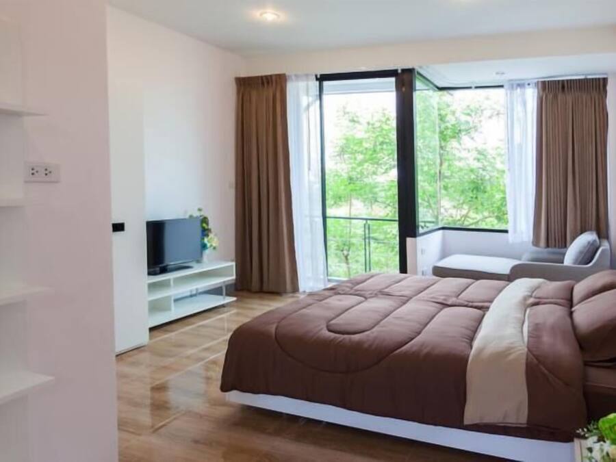 Quarto com cama, televisão em suporte e varanda com cortinas.