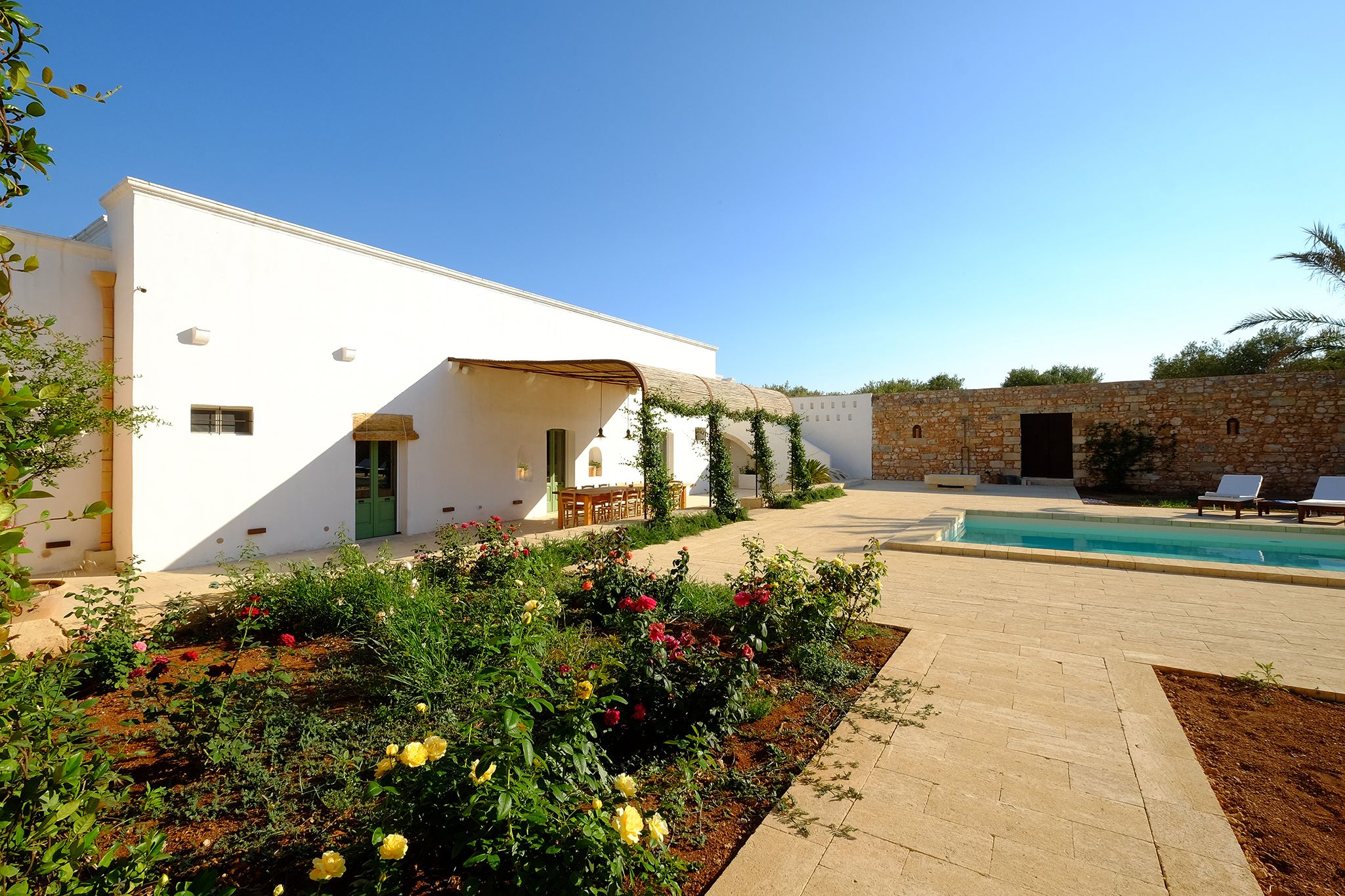 Um edifício moderno com piscina, cercado por um jardim com diversas plantas e flores.