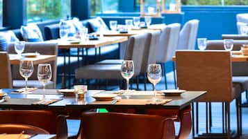 Restaurante com mesas montadas para refeições, cadeiras e luminárias pendentes.