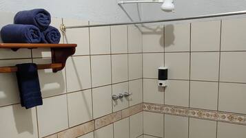 Área de duche com paredes em azulejo, um chuveiro e um porta-toalhas com toalhas.