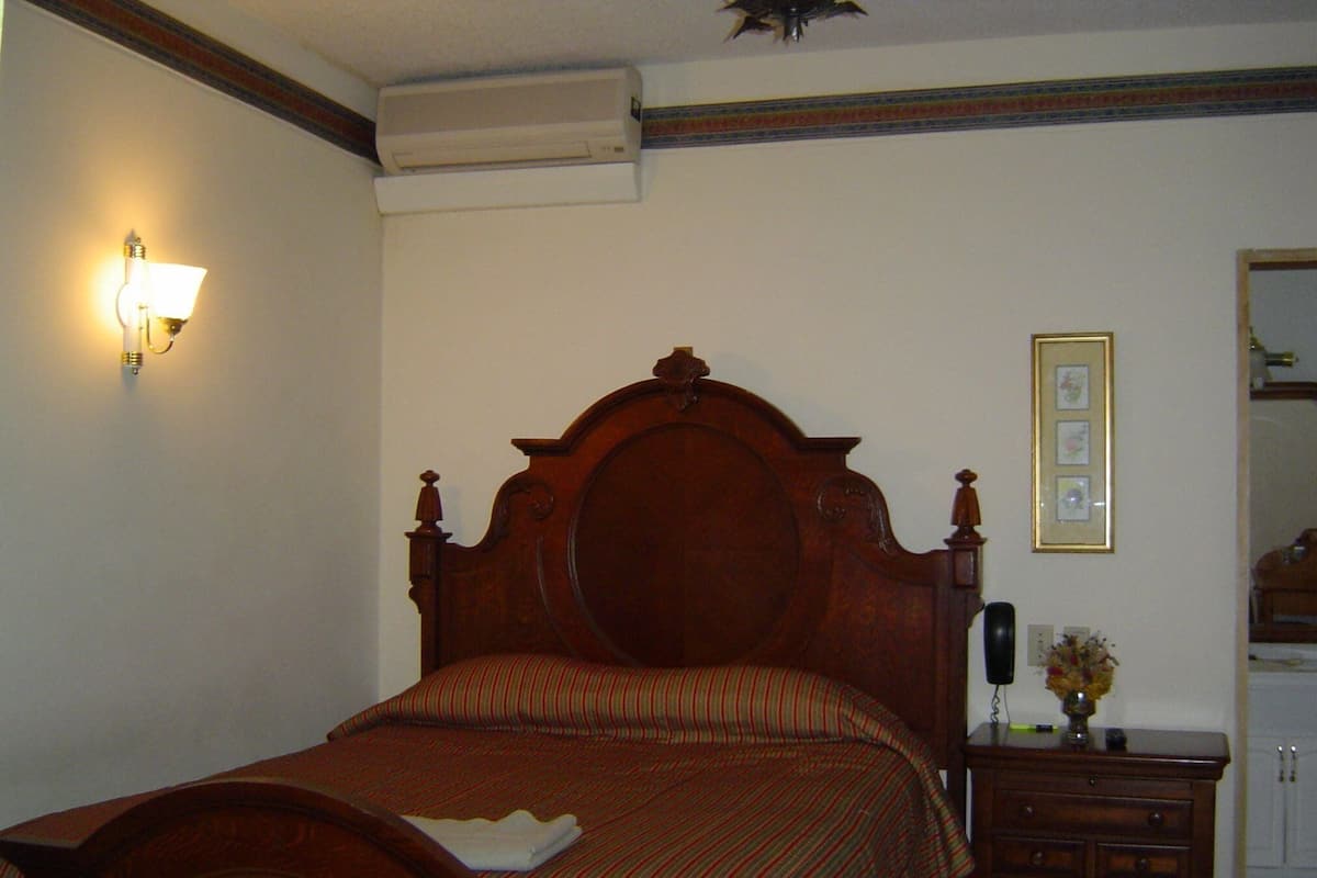 Um quarto com cama de madeira, mesa de cabeceira com um vaso, luminária na parede e um quadro emoldurado.