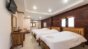 Quarto de hotel com três camas de madeira, uma cômoda de madeira, televisão fixada na parede e uma janela com persianas.