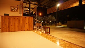 Um balcão de madeira para recepção, uma escadaria e uma área externa bem iluminada com uma árvore e uma rocha.