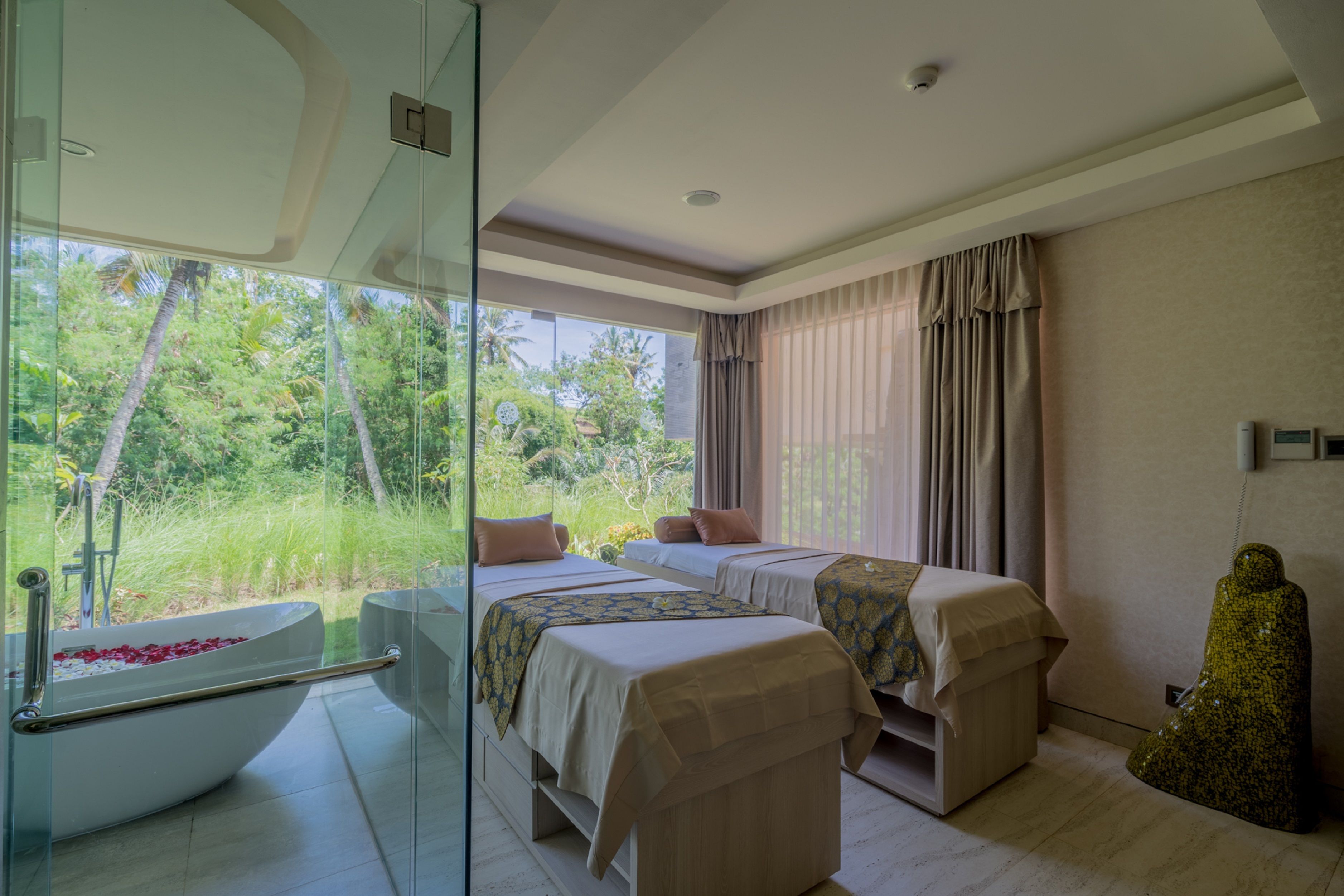 Quarto de hotel moderno com duas camas, box de vidro para o chuveiro e vista para o verde.