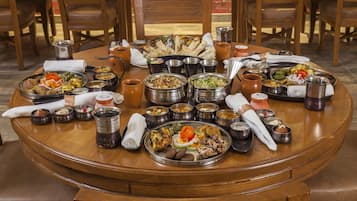 Uma mesa redonda de madeira com diversos pratos e pequenas tigelas de comida, provavelmente um buffet ou um ambiente para refeições compartilhadas.