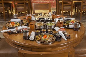 Uma mesa redonda de madeira com diversos pratos e pequenas tigelas de comida, provavelmente um buffet ou um ambiente para refeições compartilhadas.