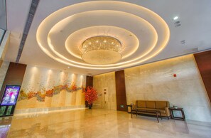 Um lobby moderno com um lustre central, uma receção e um espaço de estar.