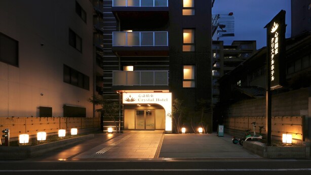 Exterior do Crystal Hotel com letreiros iluminados, entrada com portão e um caminho bem iluminado que leva às portas.