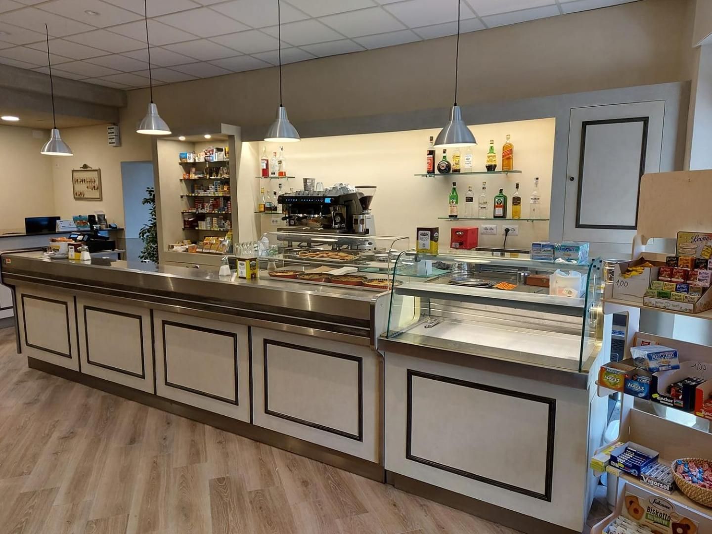 Um café com um balcão comprido, uma máquina de café e prateleiras com diversos produtos.